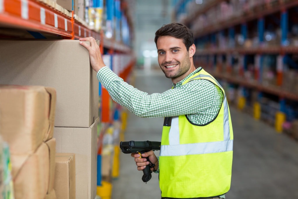 Portrait of smiling warehouse worker scanning box - Crit Suisse Portrait of smiling warehouse worker scanning box - Crit Suisse